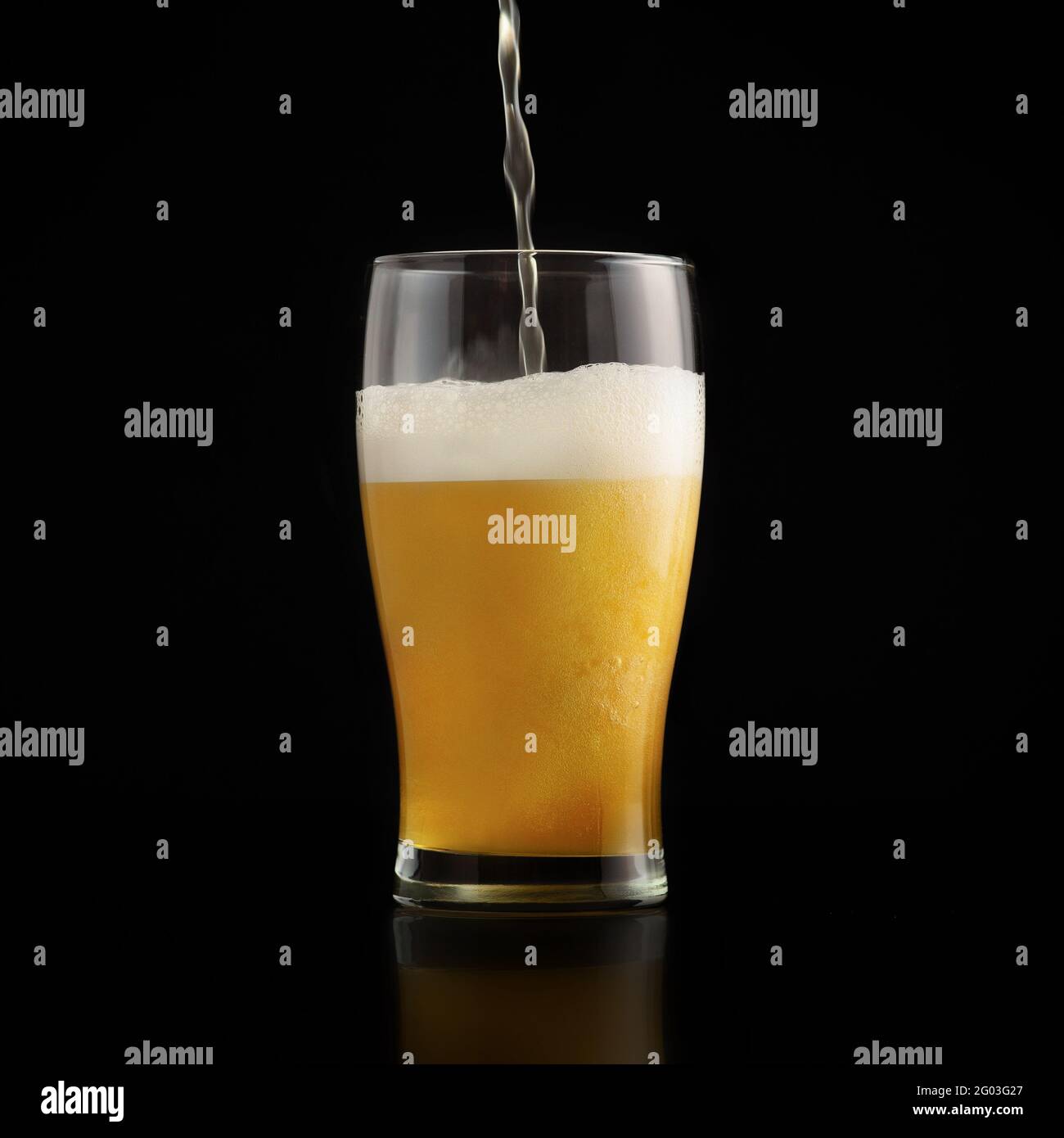 Jet of fresh light beer is poured into glass goblet on dark background ...