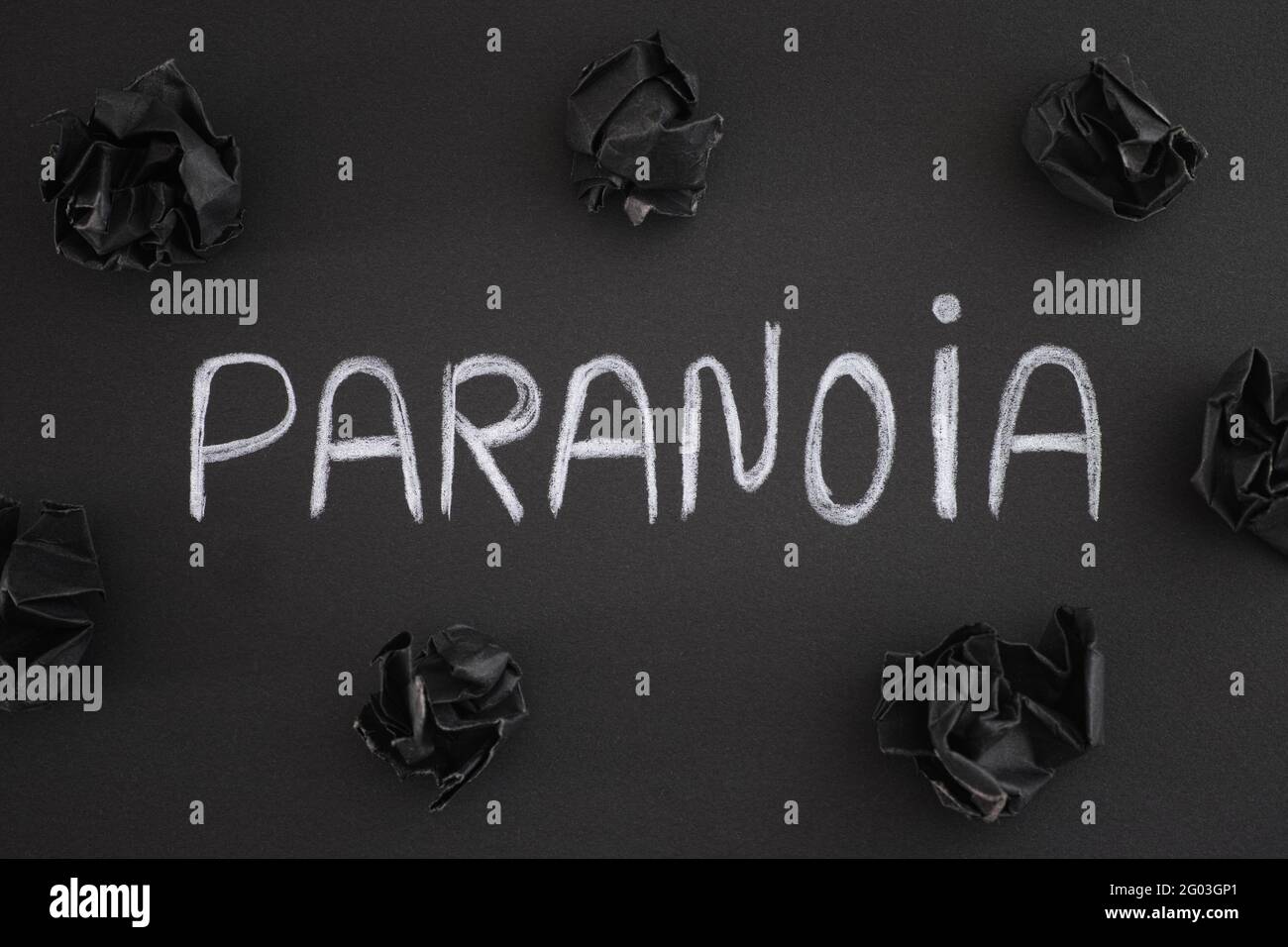 The word Paranoia on a black background with black crumpled paper balls ...