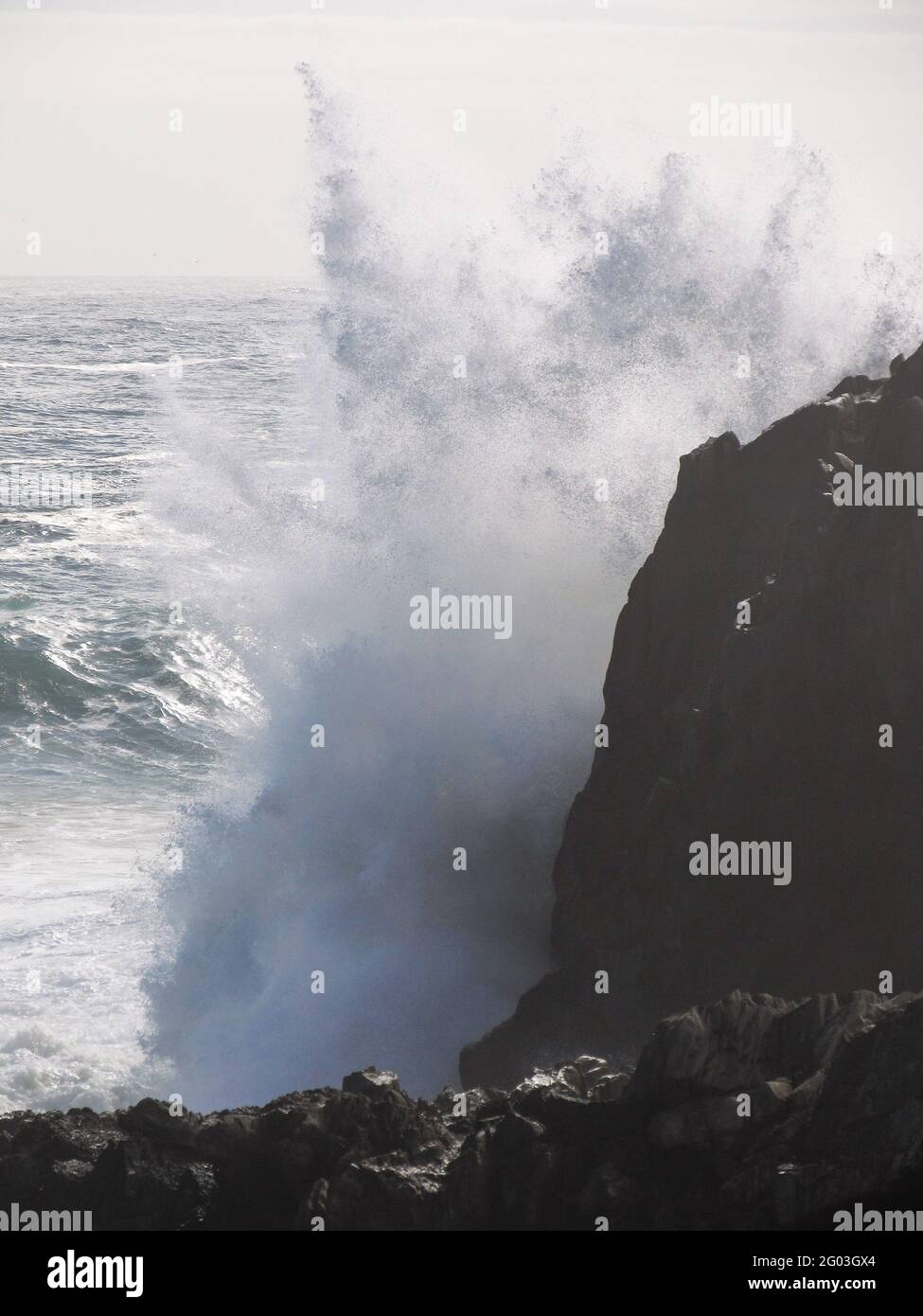 Waves breaking spectacularly against the tall, sheer, rock cliffs along ...