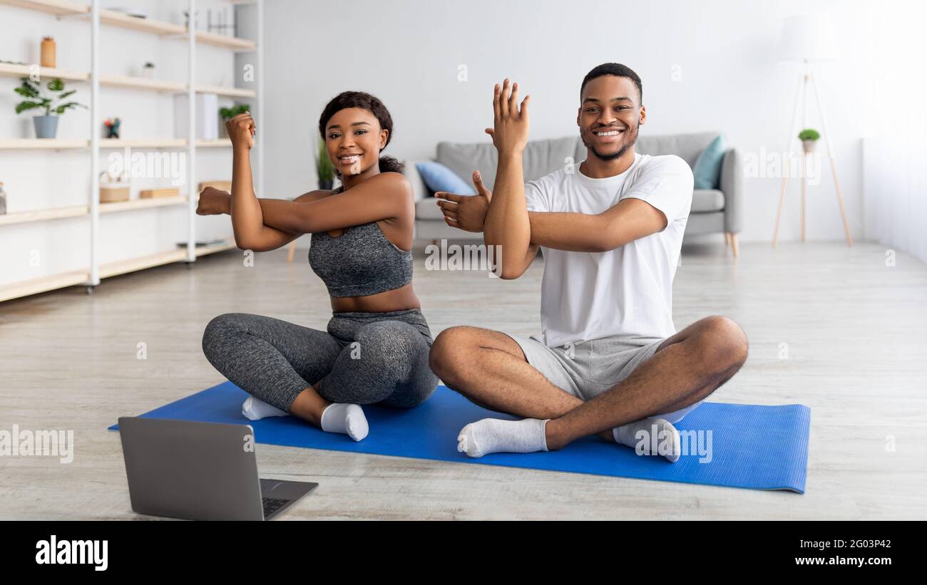 Online yoga class. Young black couple stretching arms, sitting in lotus ...