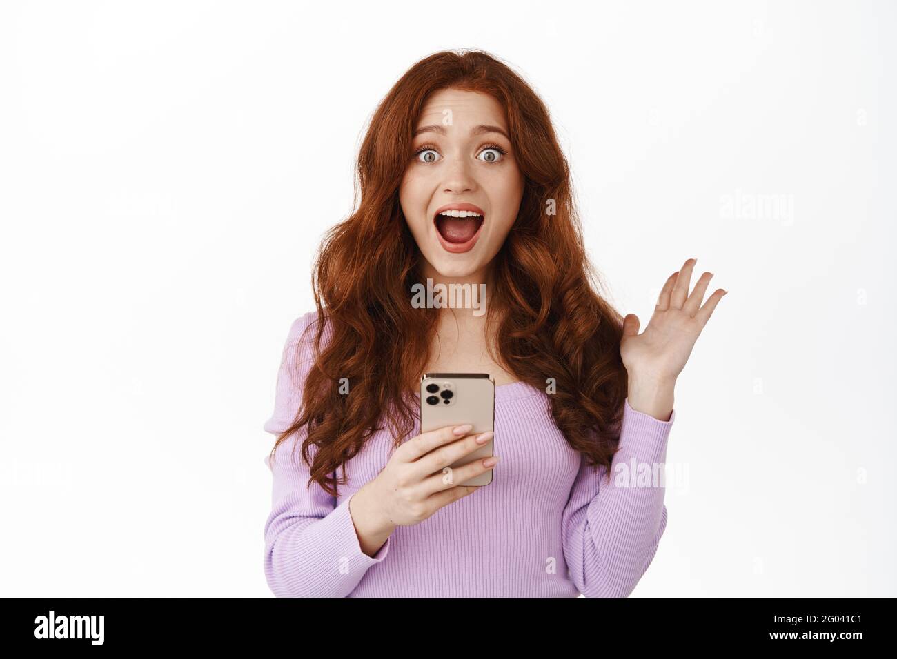 Happy ginger girl screams, holds smartphone and smiling, celebrating ...