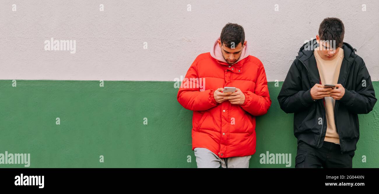young people with mobile phones leaning against the wall Stock Photo ...
