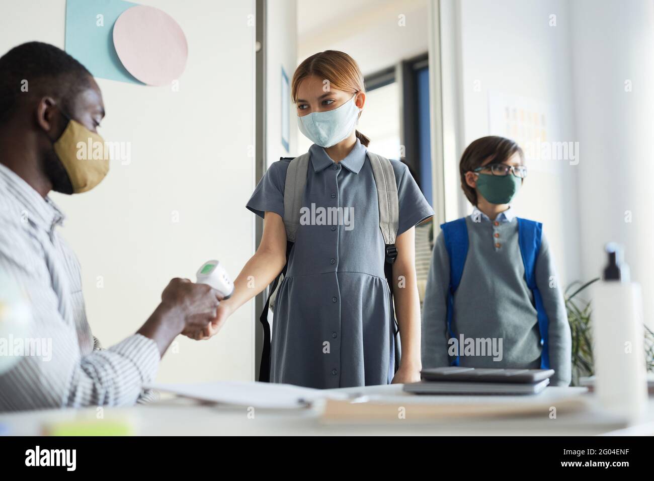 Portrait of male teacher checking temperature of children entering ...