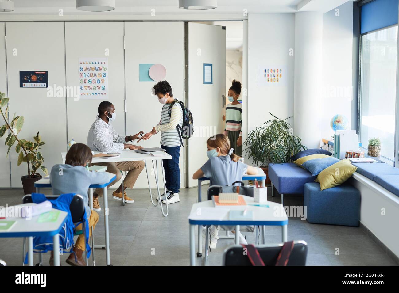 Wide angle portrait of male teacher helping children sanitizing hands ...
