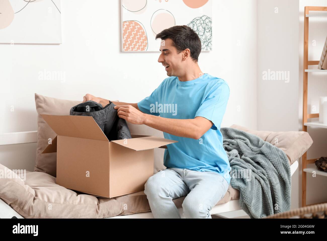 Surprised young man unpacking box with clothes at home Stock Photo - Alamy