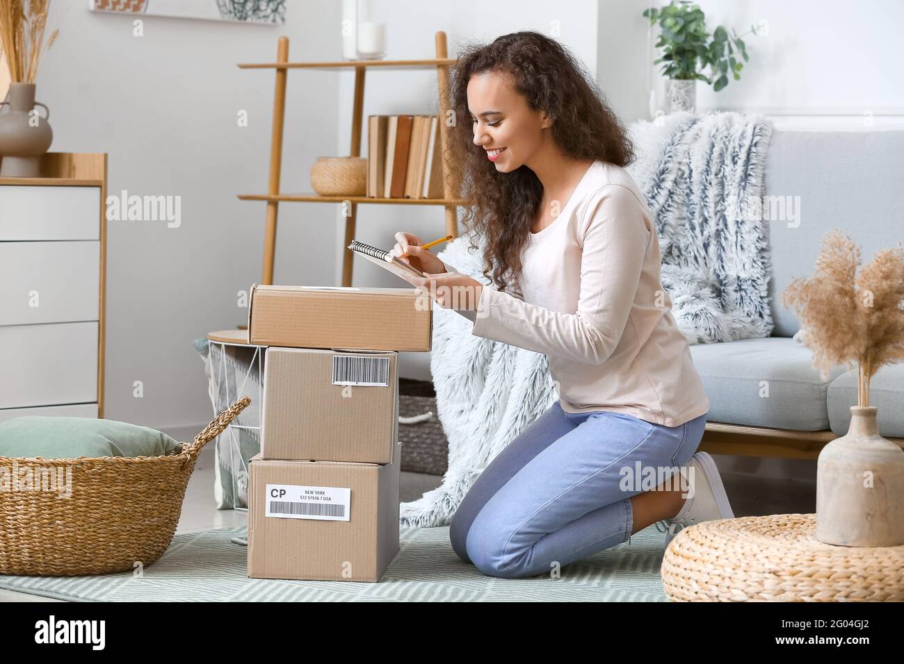 Young woman with parcel writing in notebook at home Stock Photo - Alamy