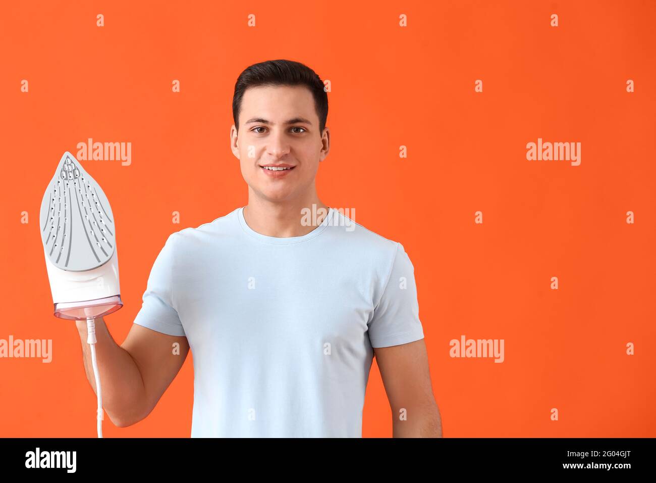 Handsome young man with iron on color background Stock Photo - Alamy