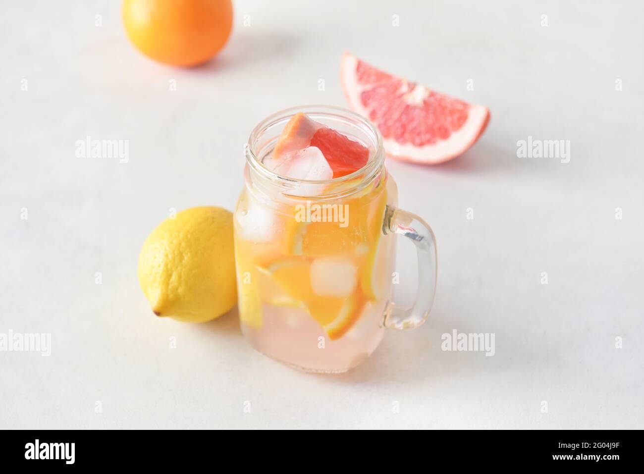 Mason jar of tasty cold lemonade and citrus fruits on light background ...