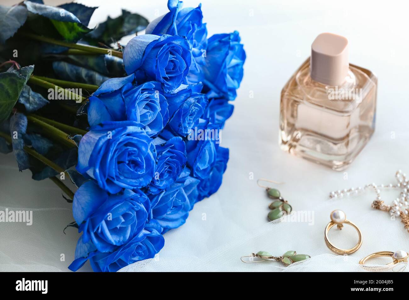Beautiful blue roses, perfume and jewelry on light background Stock ...