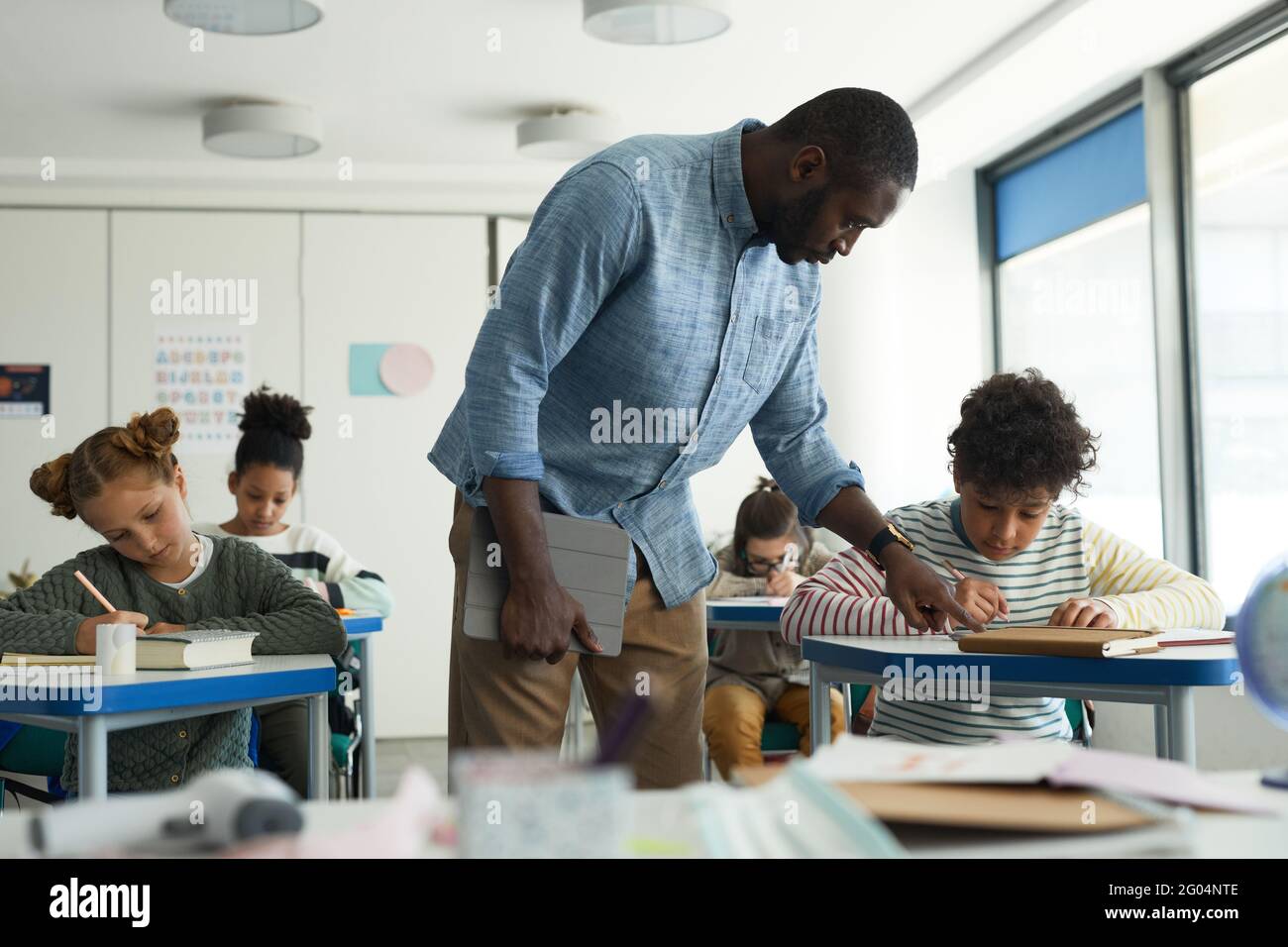 Portrait of male African-American teacher helping kids in school ...