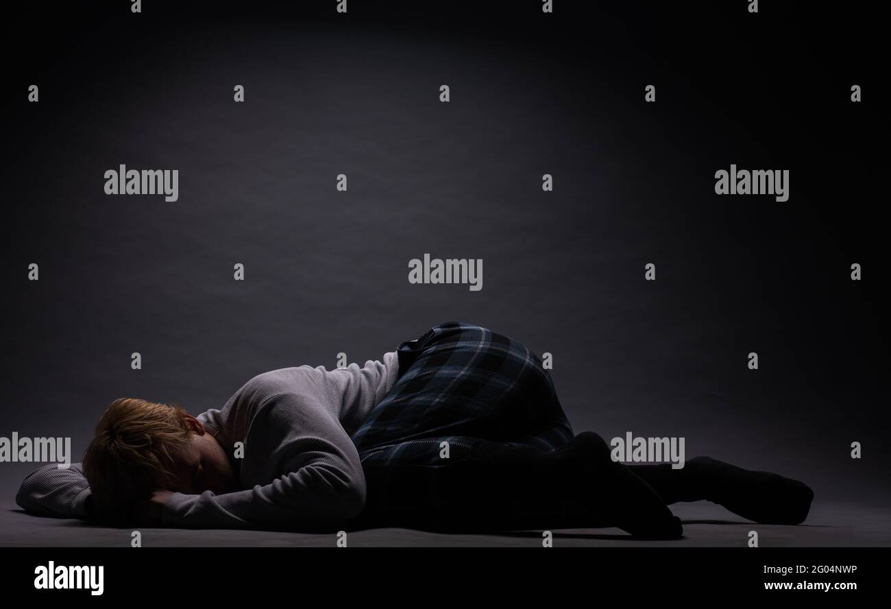 Depressed and sad boy is laying on the ground while suffering from the ...