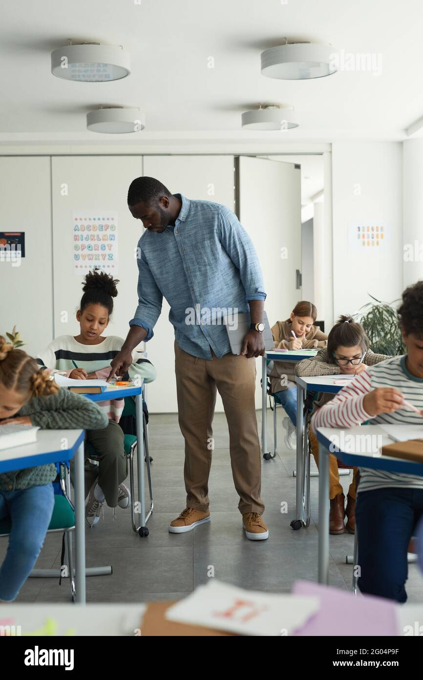 Vertical full length portrait of male African-American teacher helping ...