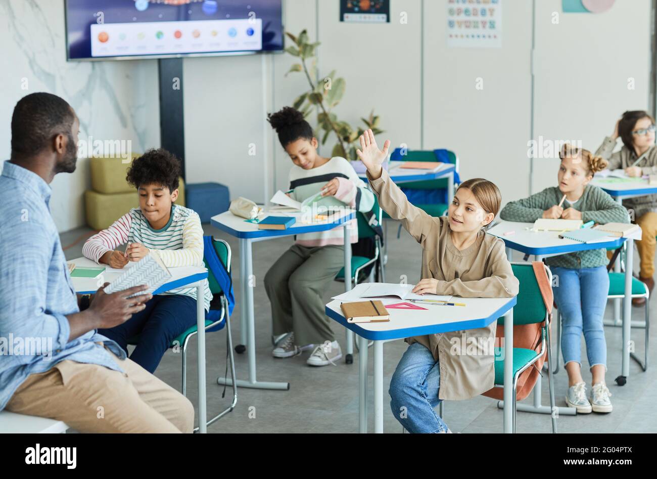 Diverse group of children in school classroom with smiling girl raising ...