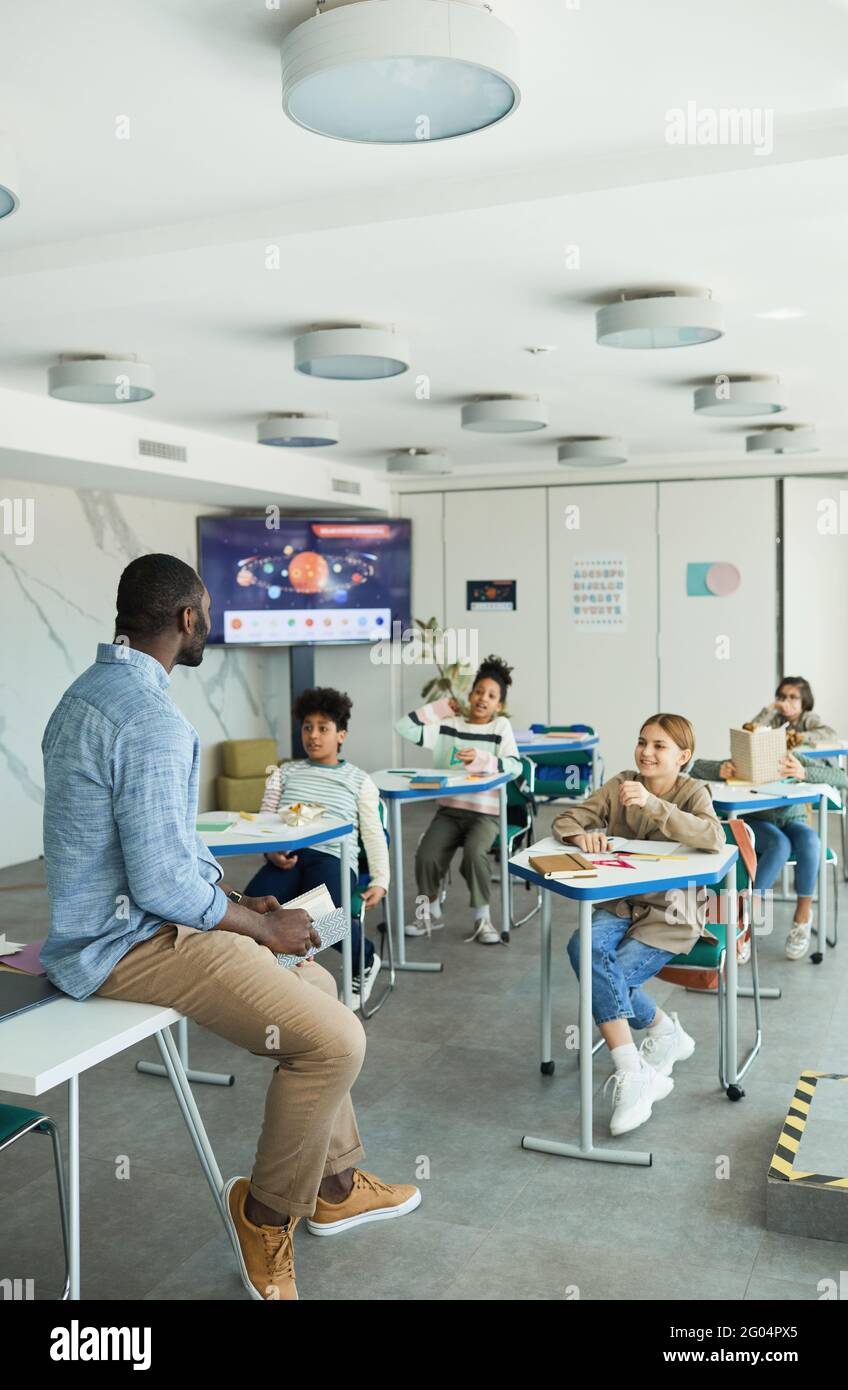 Back view portrait of male teacher talking to diverse group of kids in ...