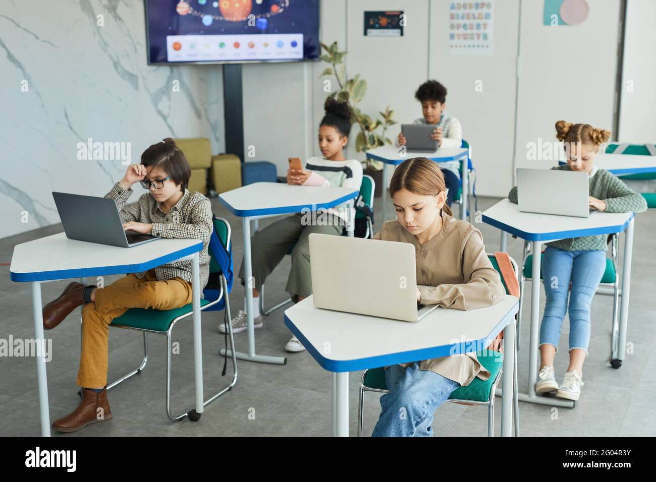 Diverse group of young children using laptops while sitting at desks in ...