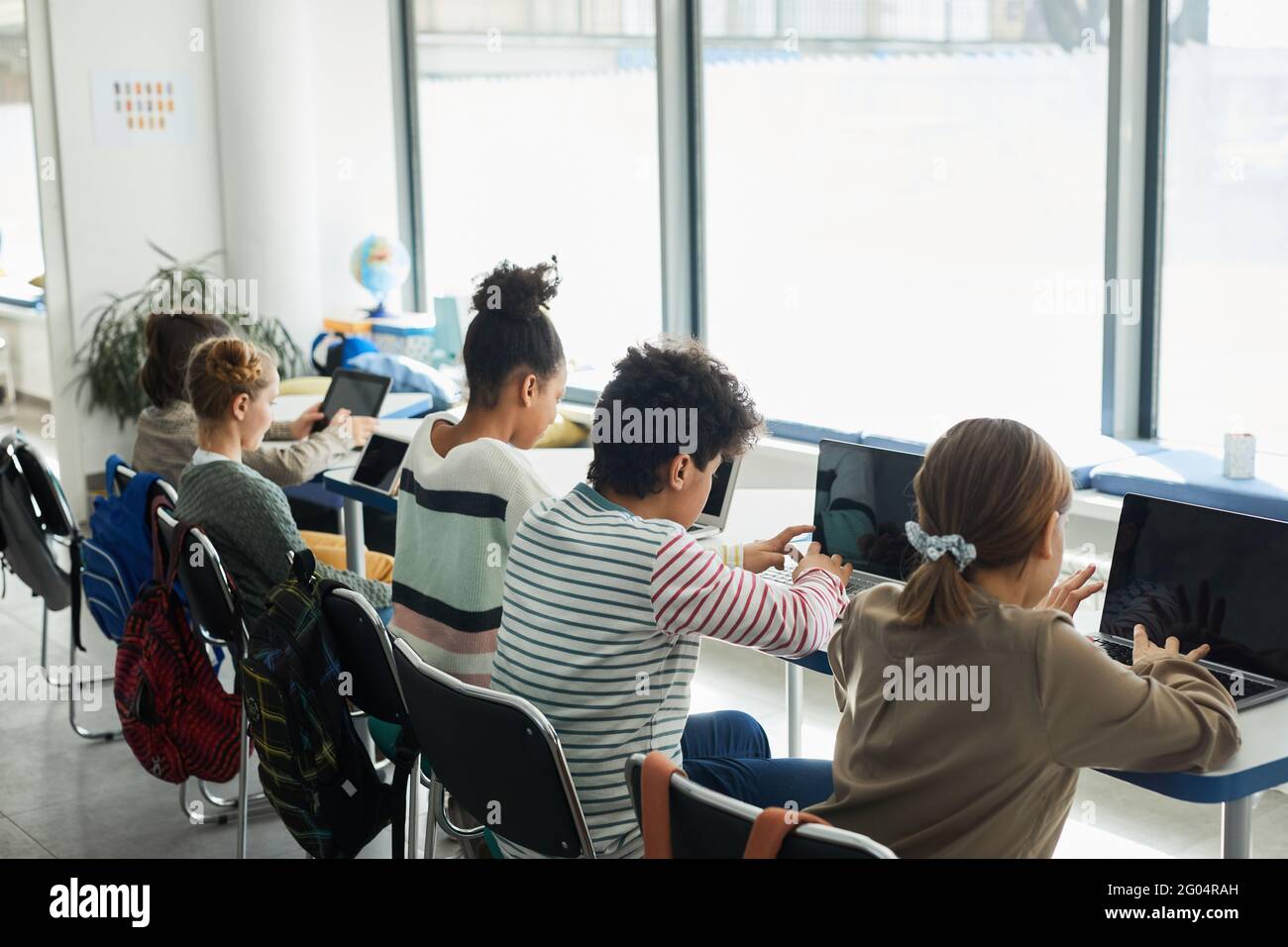 Back view at diverse group of children sitting in row at school ...