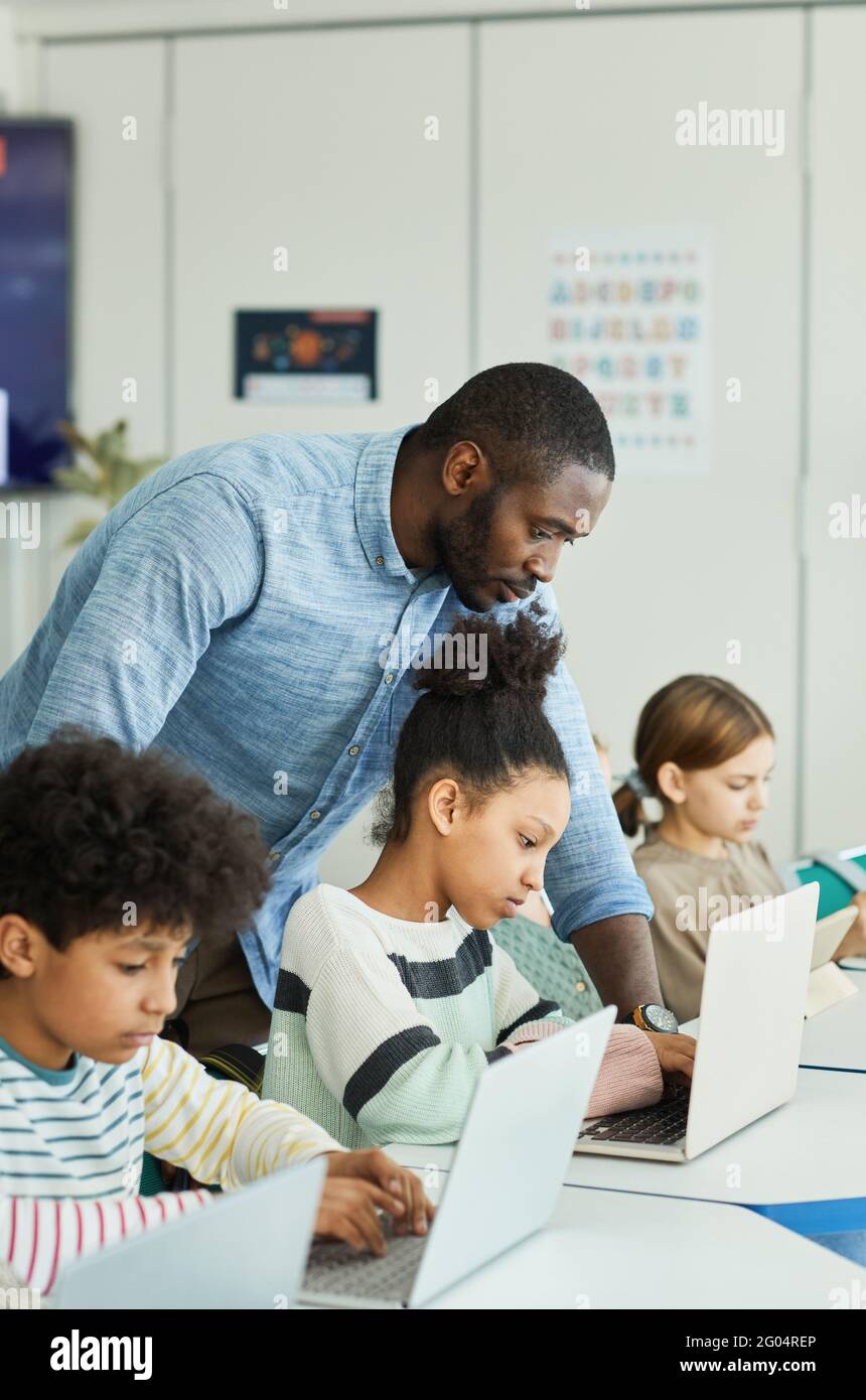 Side view portrait of male teacher helping children using computers in ...