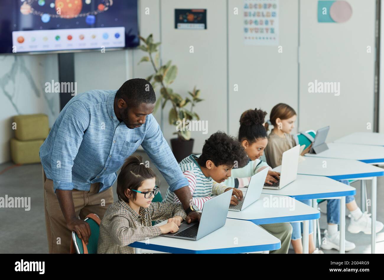 Side view portrait of male teacher helping children using computers in ...