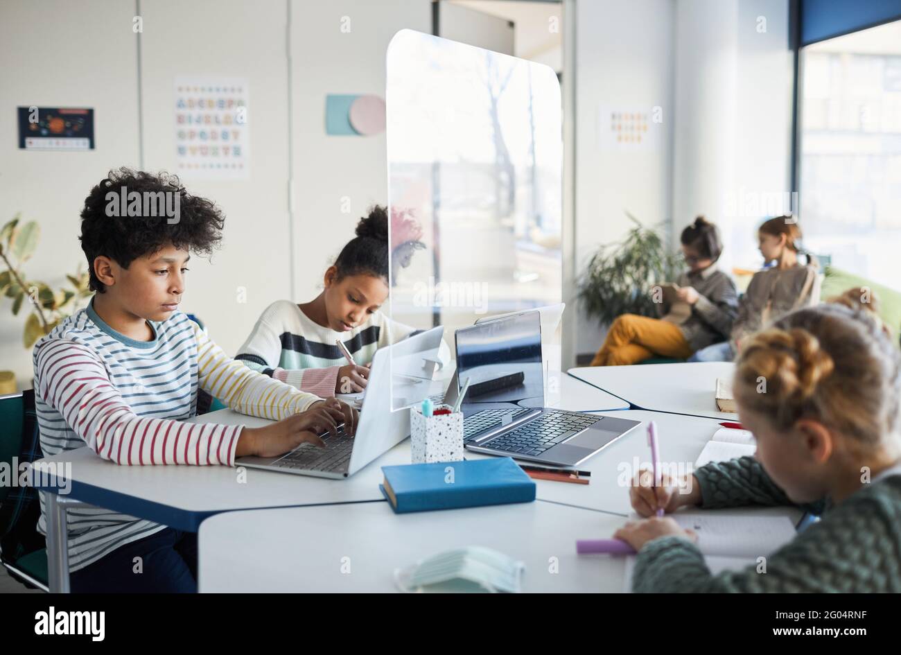 Diverse group of children working together at desk in classroom with ...