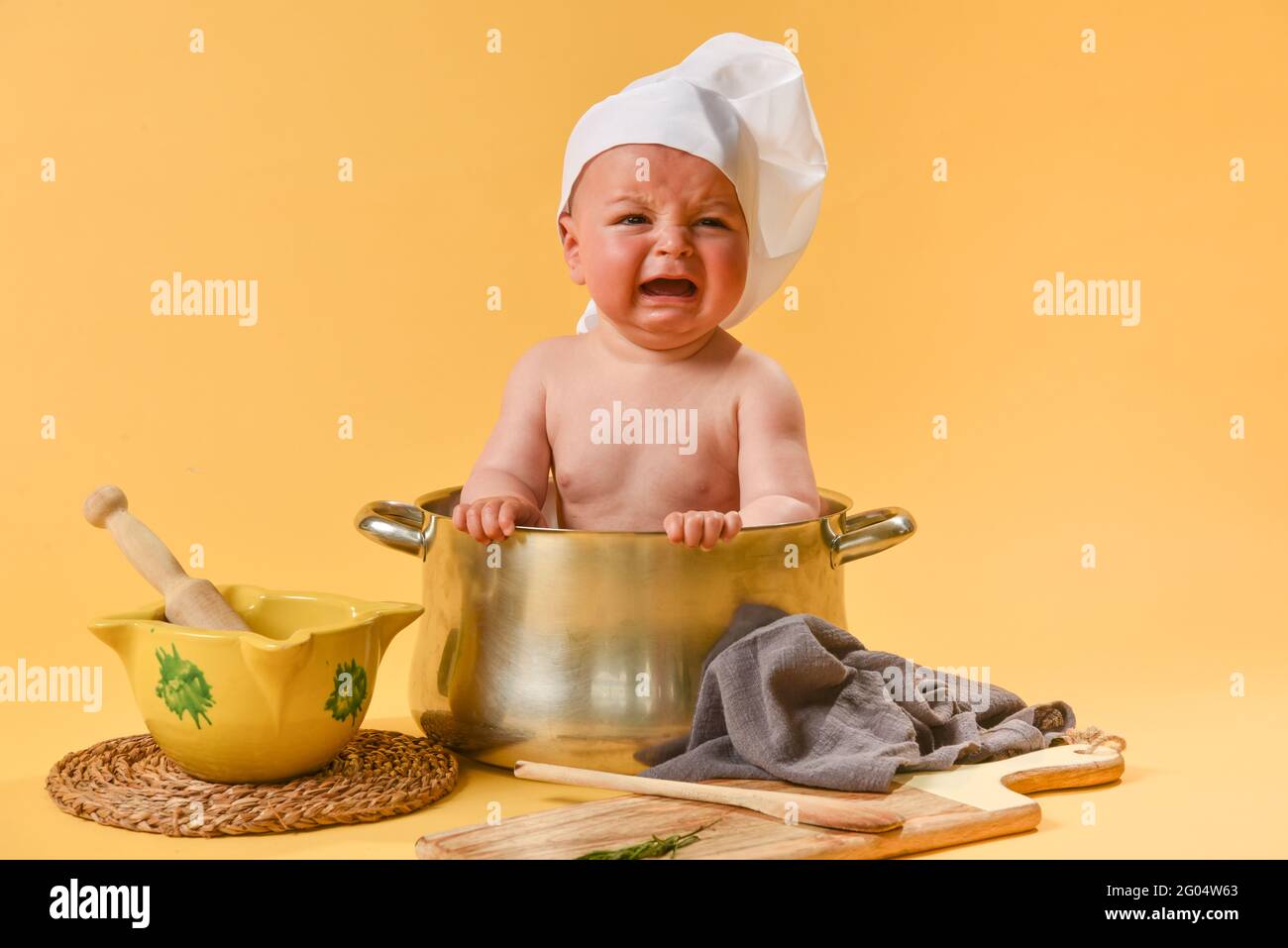 Crying cute baby tucked inside a pot with a chef's hat and cooking ...
