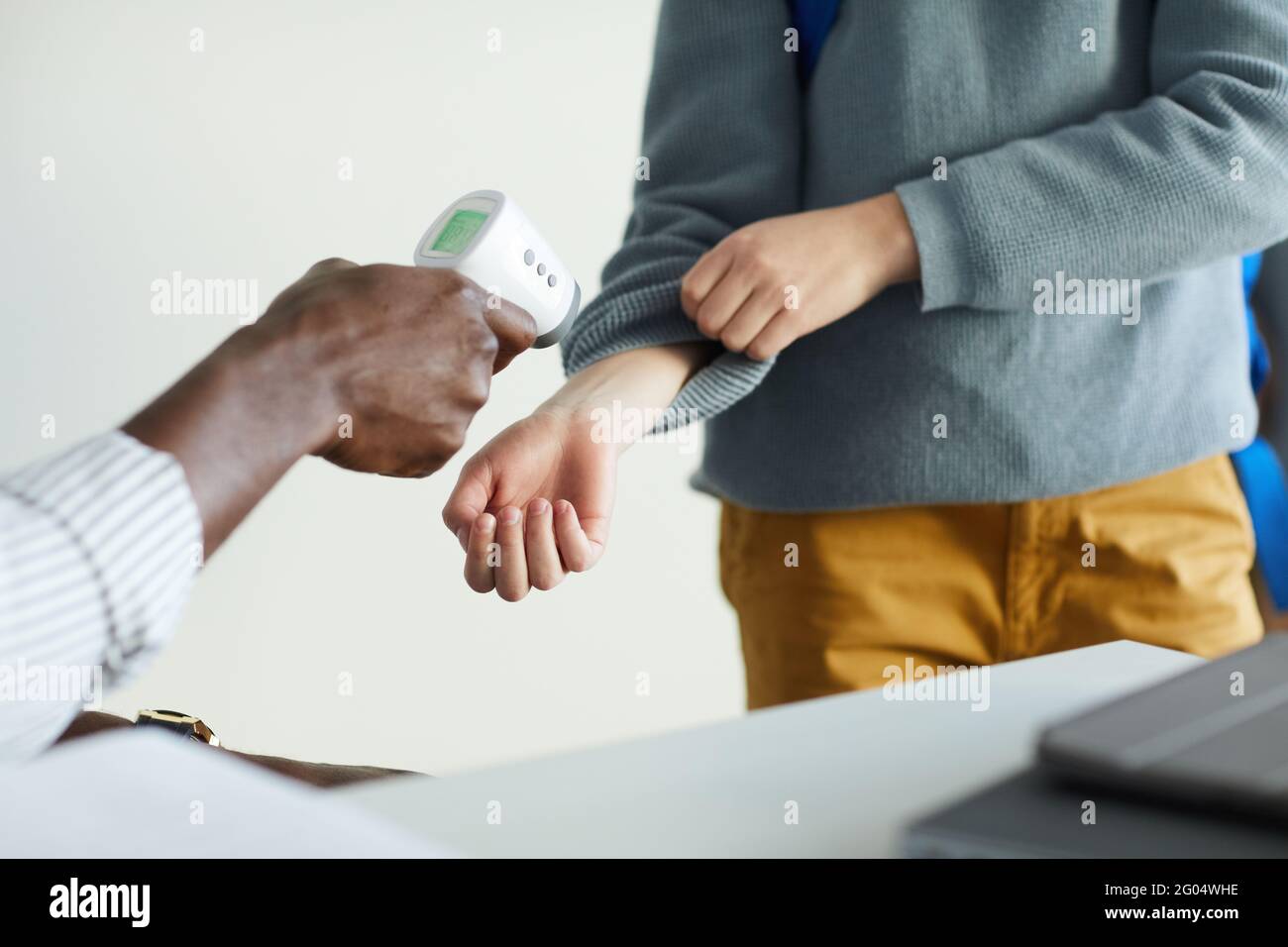 Close up of male teacher checking temperature of children entering ...