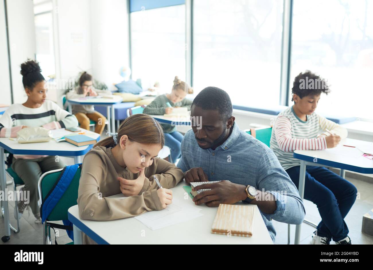High angle portrait of caring male teacher helping young girl in school ...
