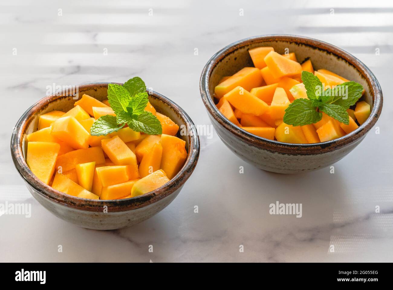 Cantaloupe melon bite-sized cubes close up in a bowls on light marble ...