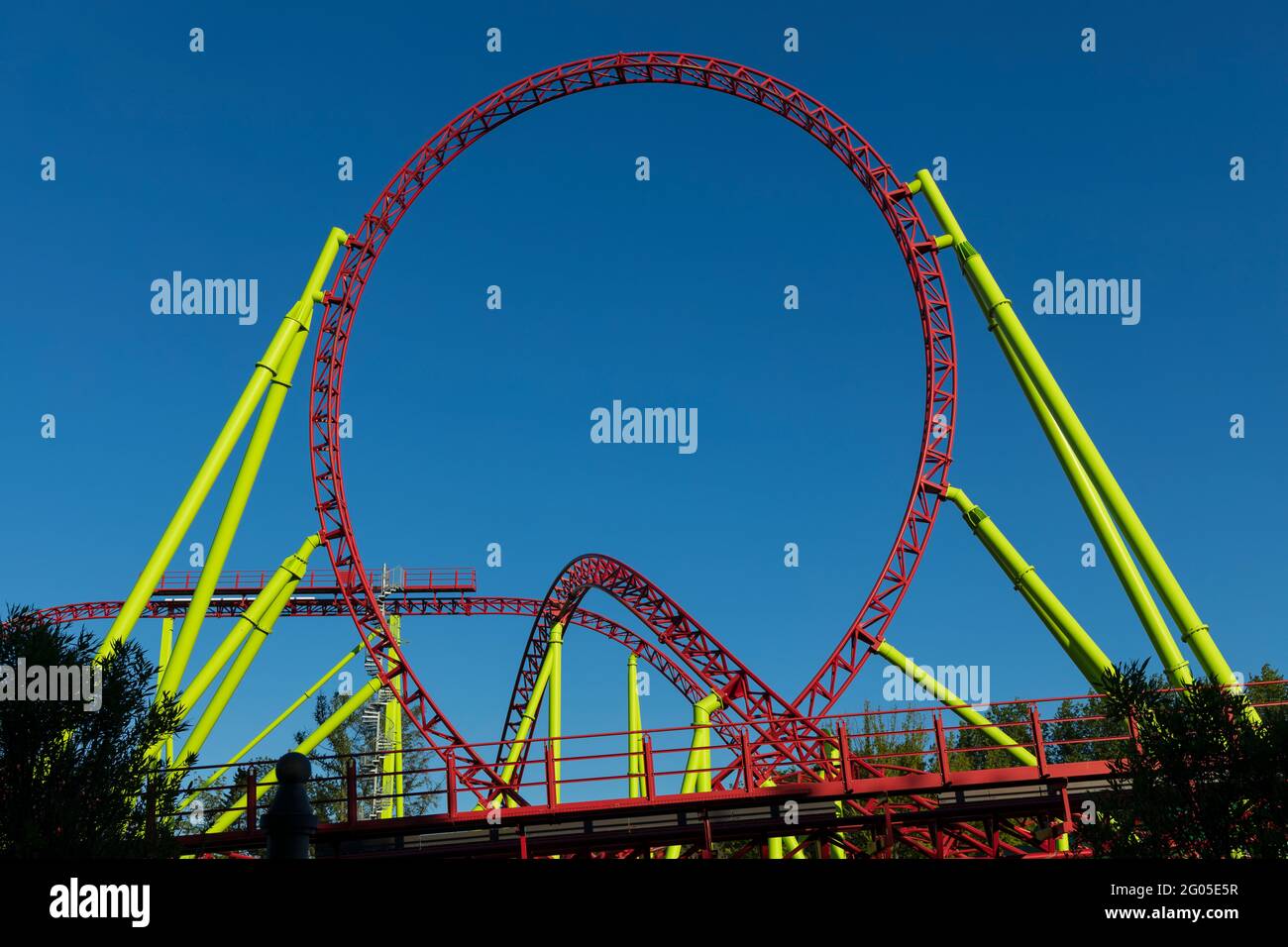 Red roller coaster loop with yellow pillars on blue sky background ...