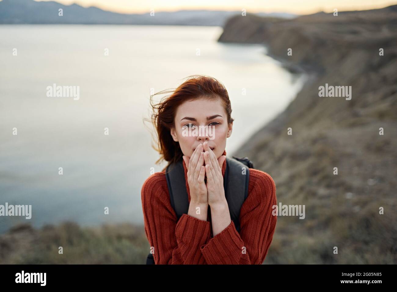a traveler in a sweater holds her hands near her face on nature in the ...