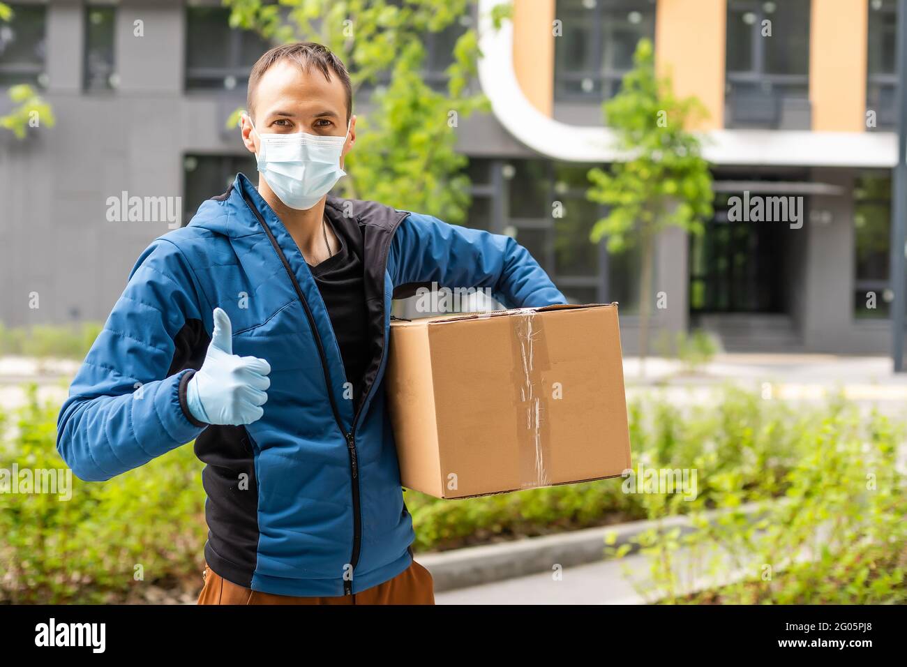 Hispanic young delivery man wearing face mask while carrying parcel box ...
