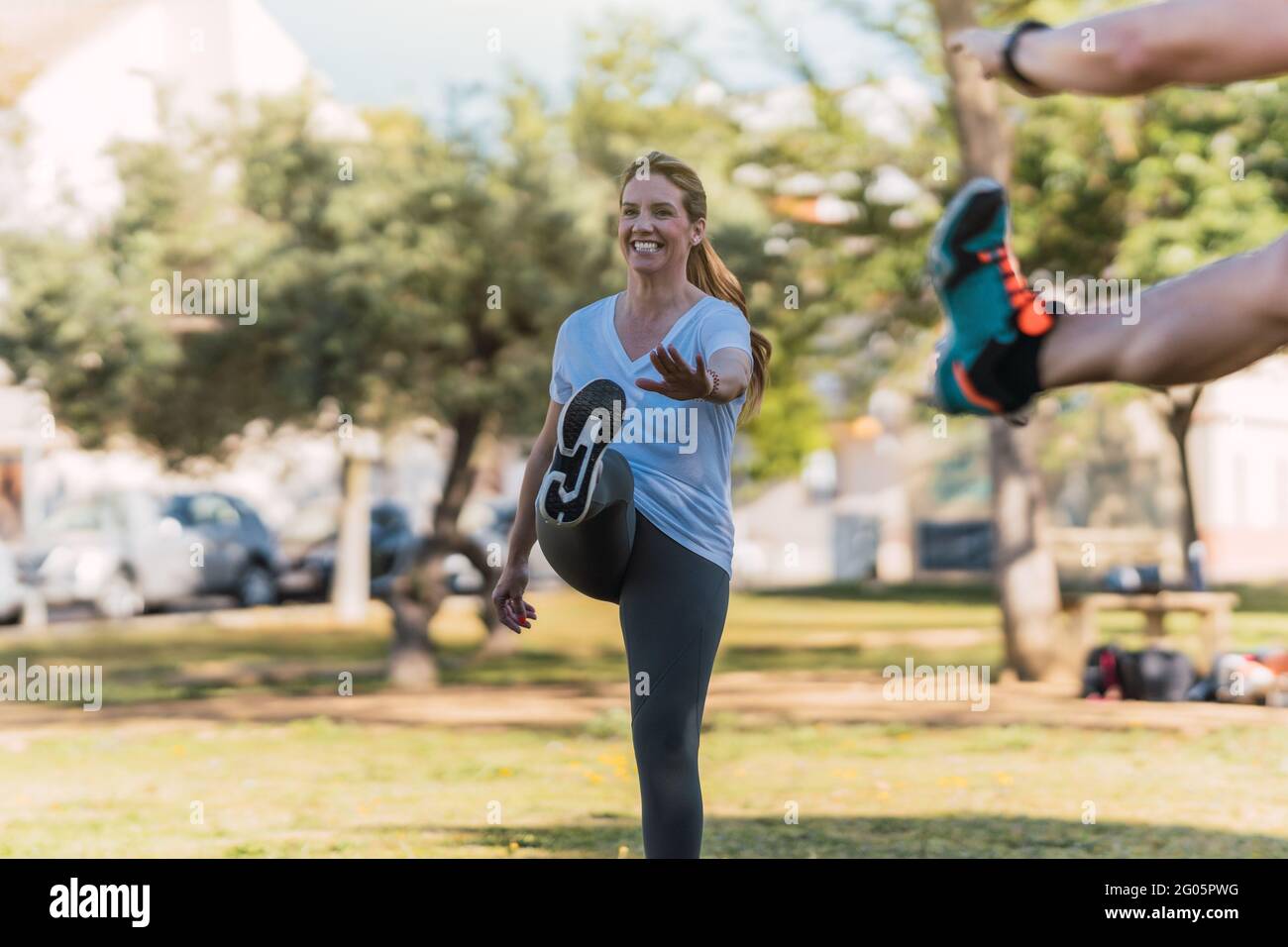 Blonde woman in sportswear smiling as she lifts her leg to warm up in a ...