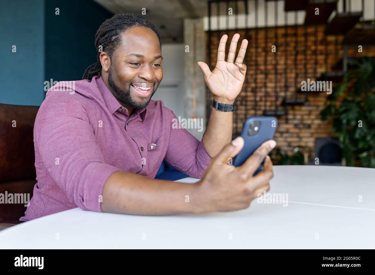 Happy African-American guy holding smartphone and gesturing hello ...
