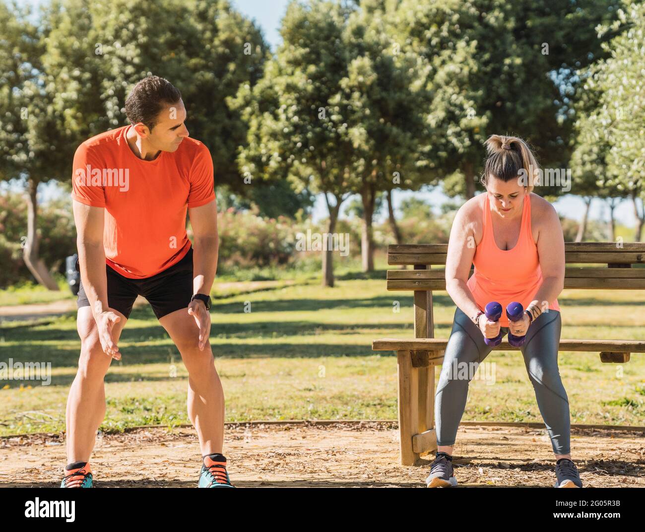 Personal trainer guiding a woman to exercise with weights in a park ...