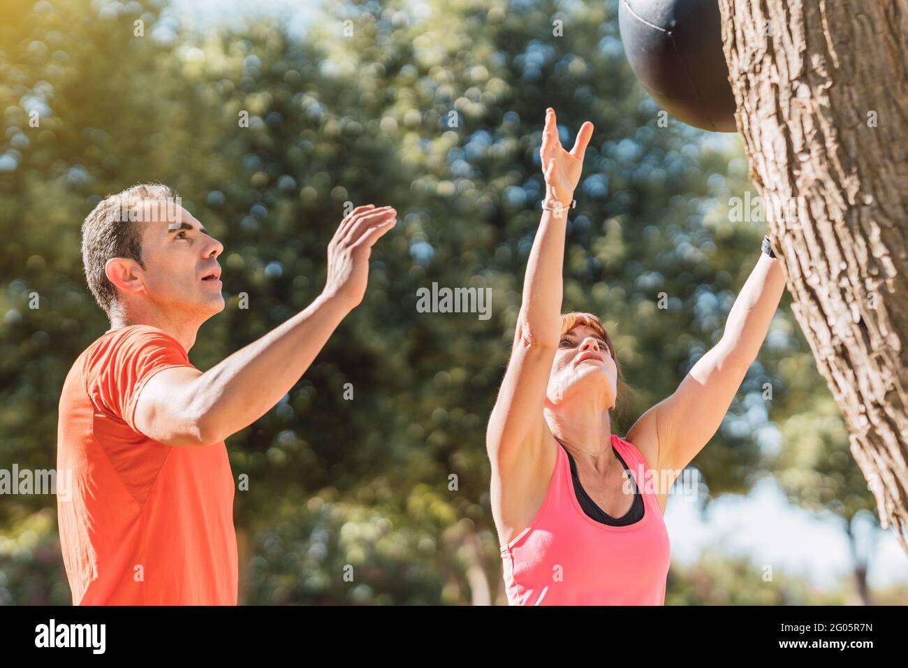 A woman throwing a medicine ball against a tree with the help of a ...