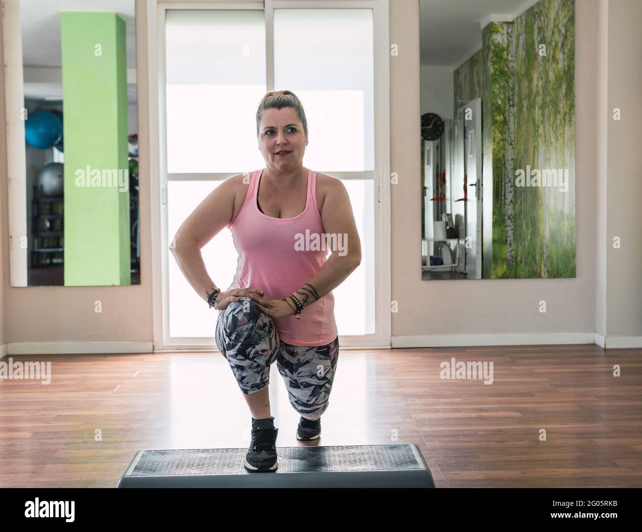 Blonde woman in sportswear doing front splits with a stepper in a room ...