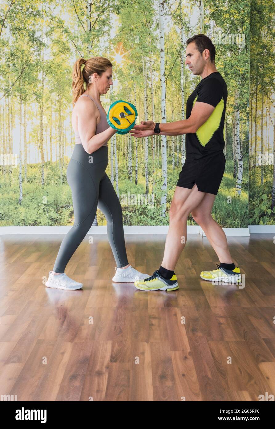 Vertical photo of a personal trainer helping a woman to do weights in a ...