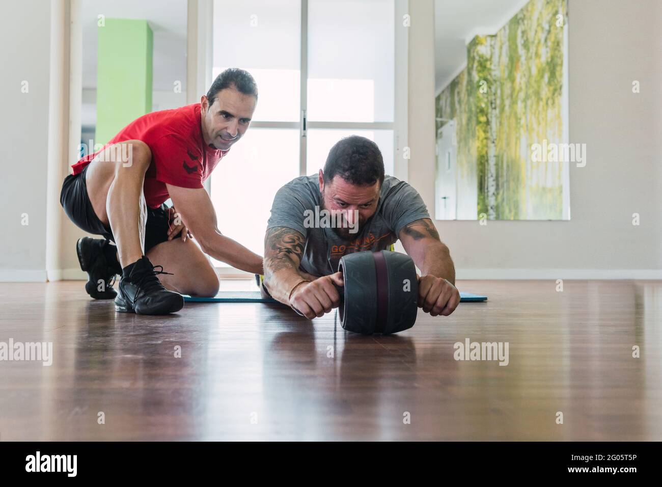 Coach helping a man to do exercise with an abs roller in a gym Stock ...