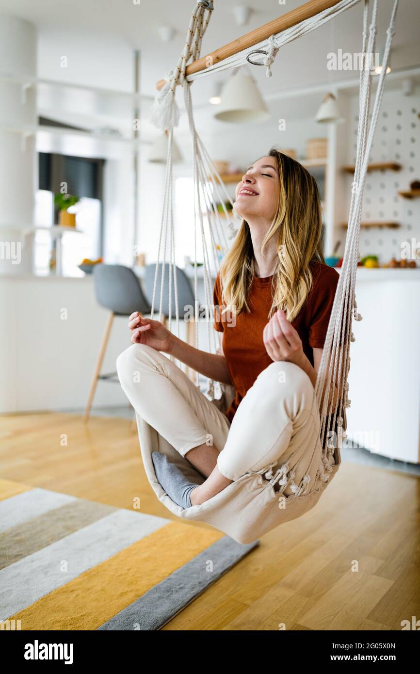 Young woman chilling at home in comfortable hanging chair in front of ...
