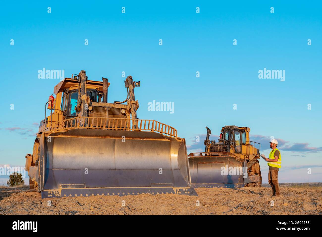 construction worker next to heavy machinery two yellow excavators at a ...