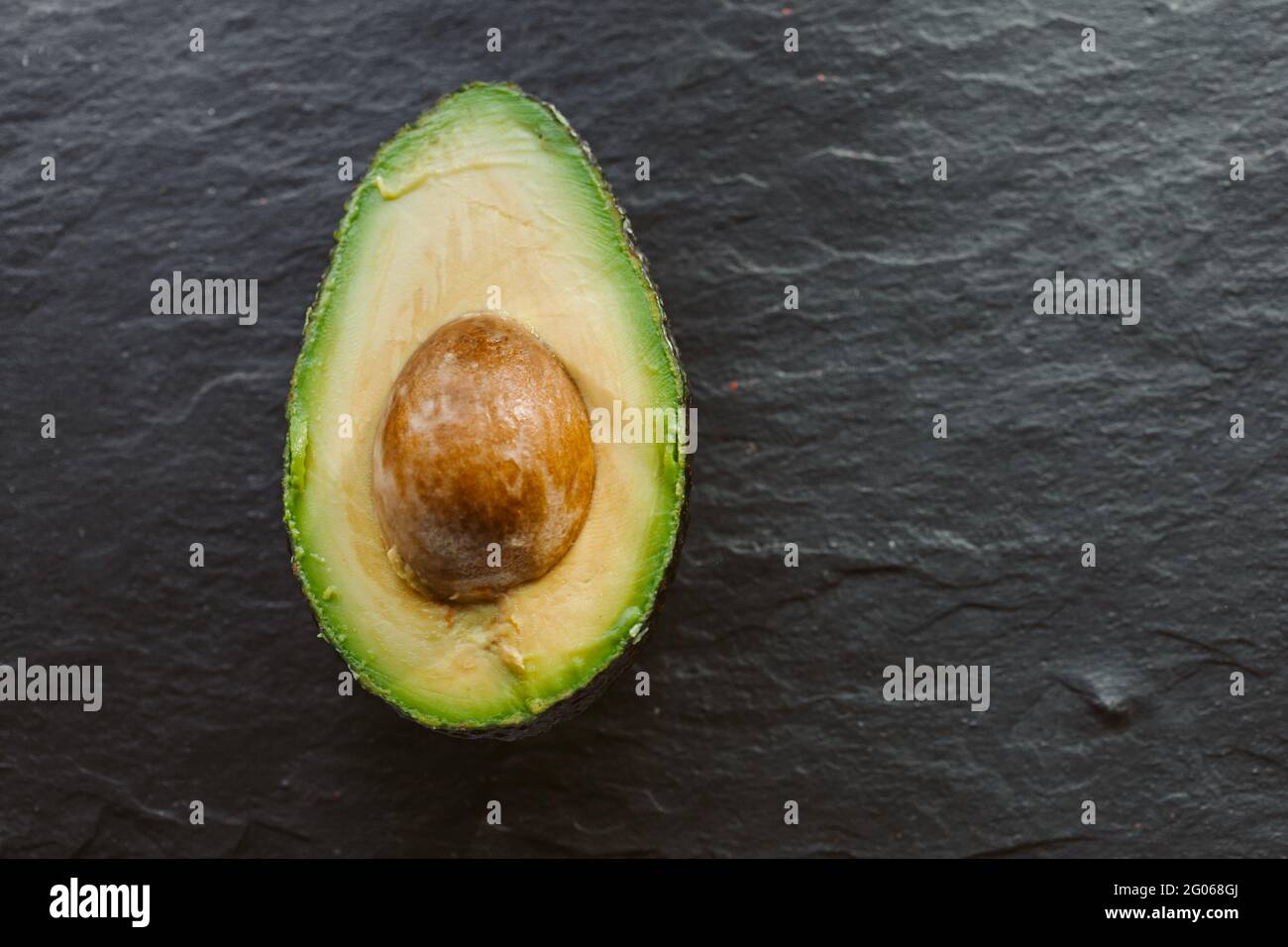 Close up of avocado cut in a half on black slate background. Avocado ...