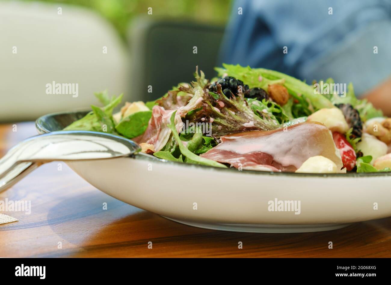 Delicious salad with prosciutto jamon on a white plate at a wooden ...
