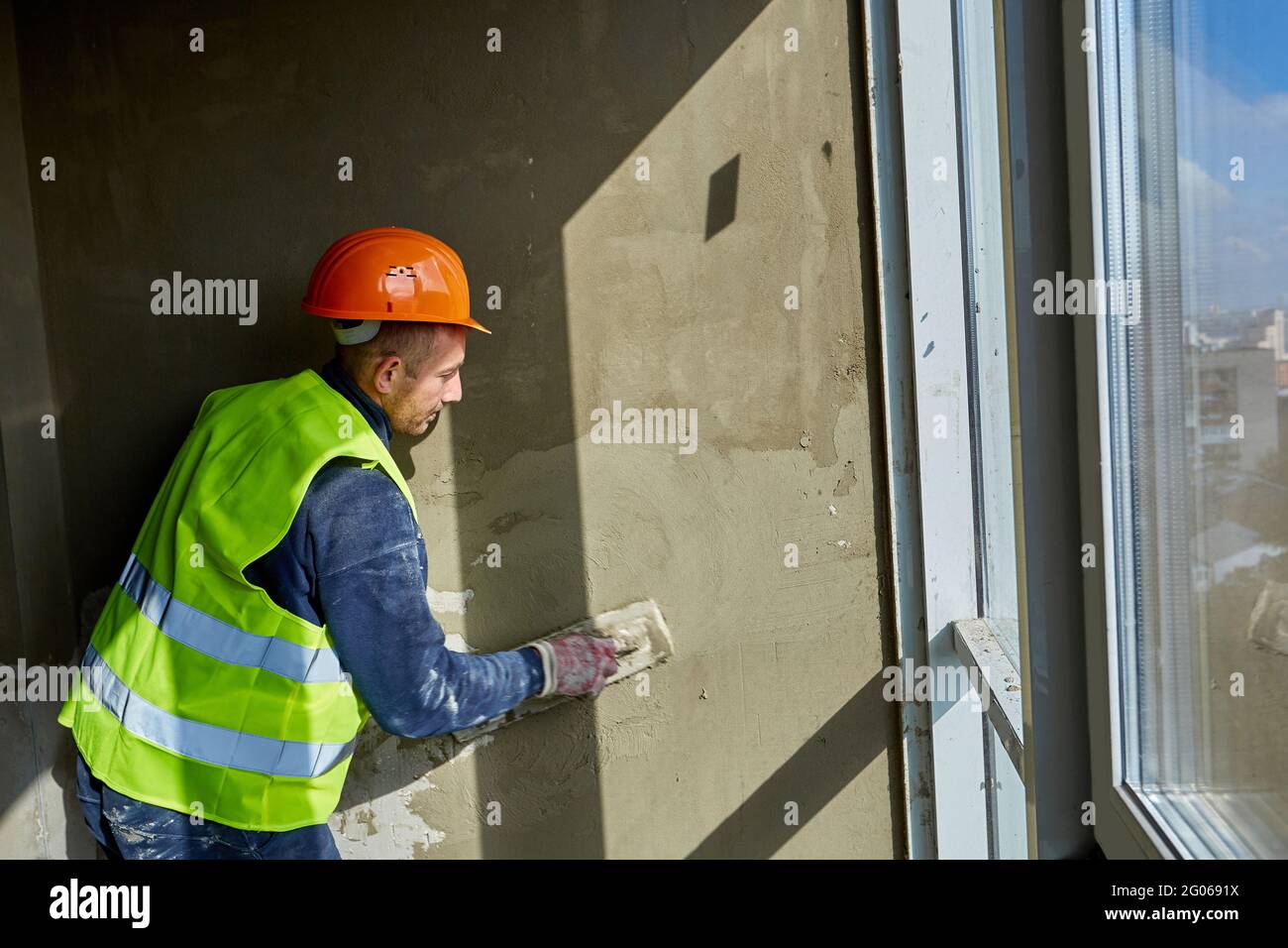 Worker in workwear and safety helmet is putting putty on wall, using ...