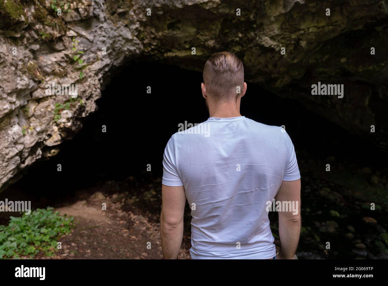Young man standing in front of a cave entrance and looking into the ...