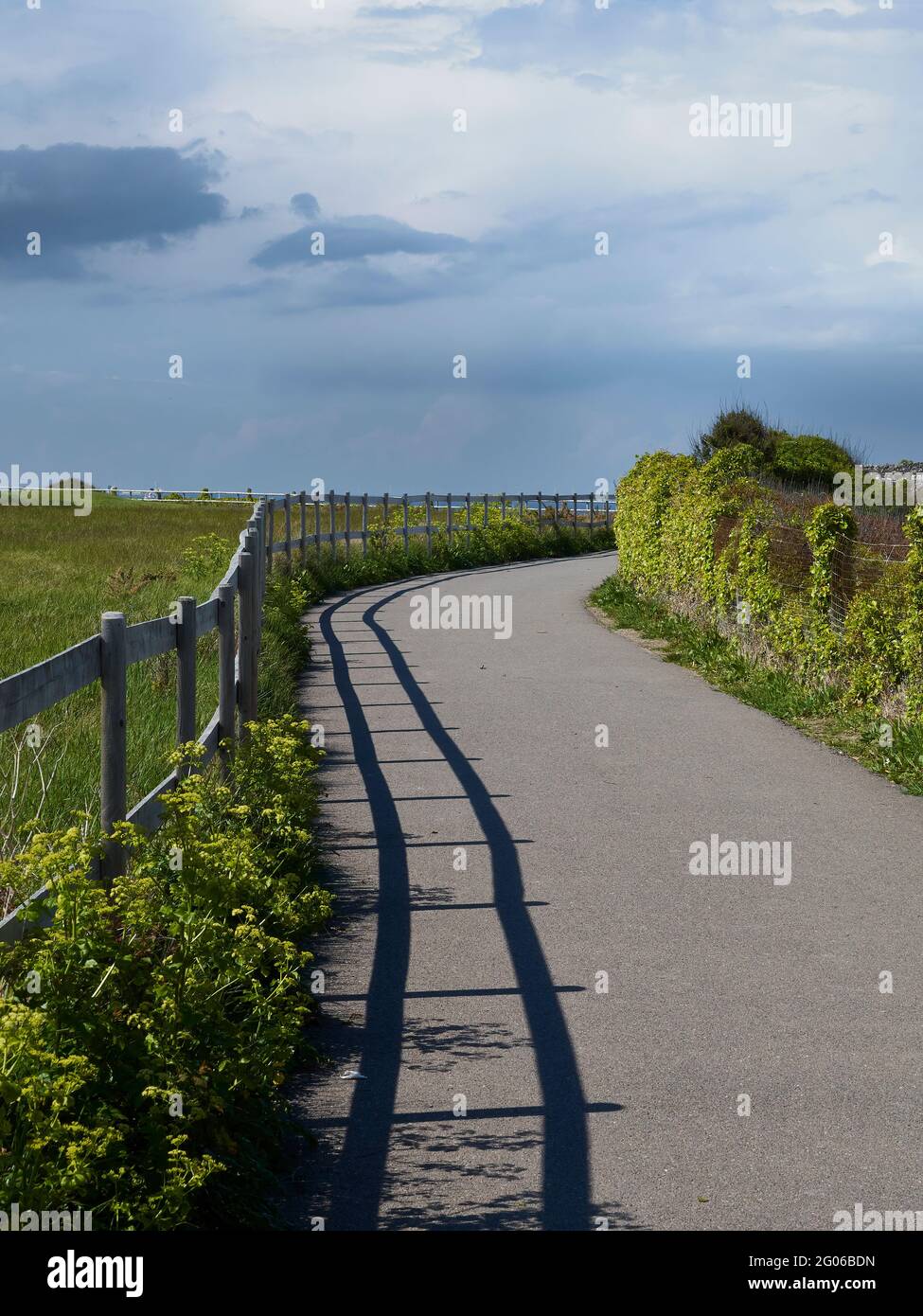 A meandering, sunlit, cliff-top path between fields, hedges and under a ...