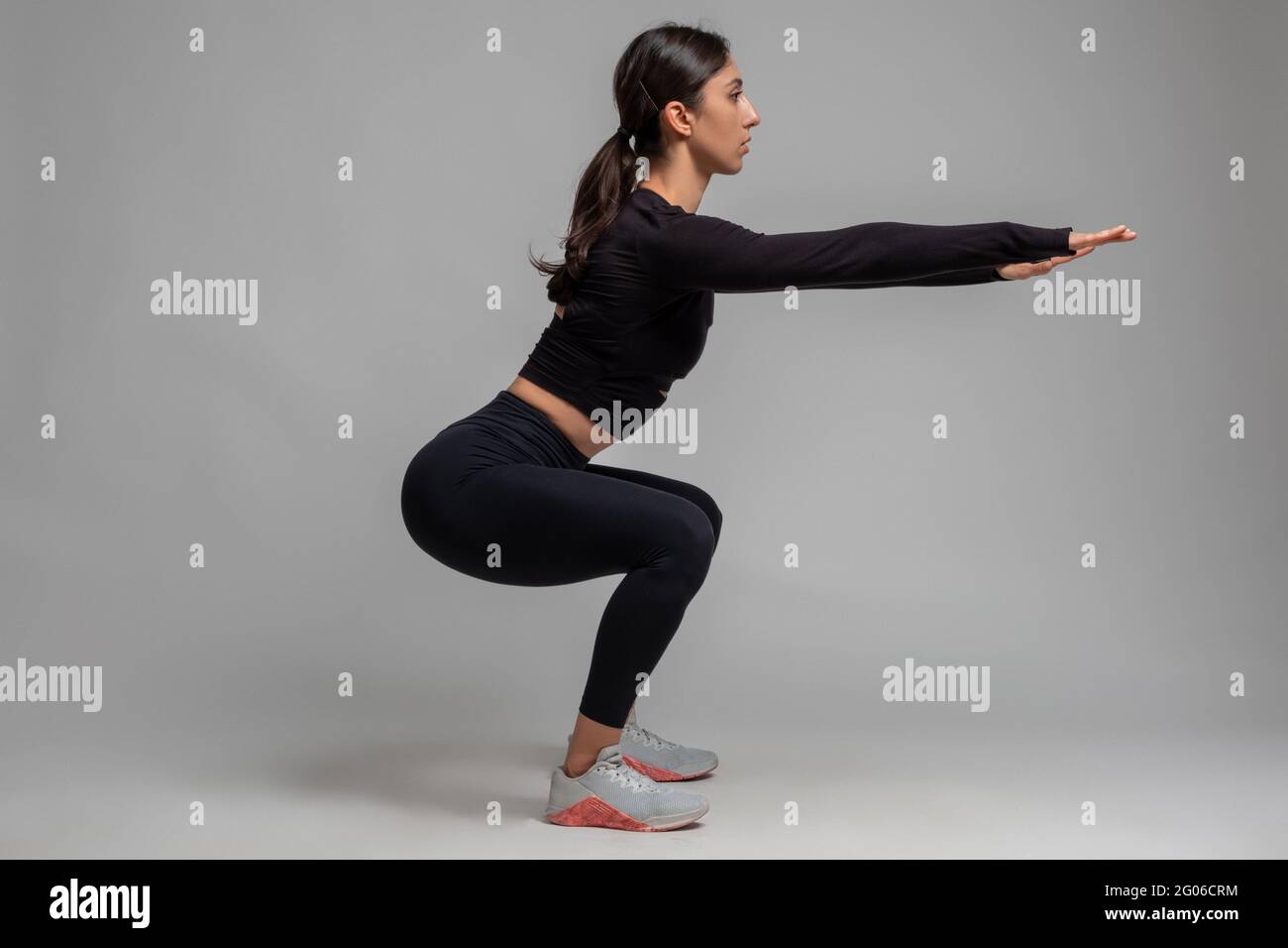 Side view of girl doing squats on grey background Stock Photo - Alamy