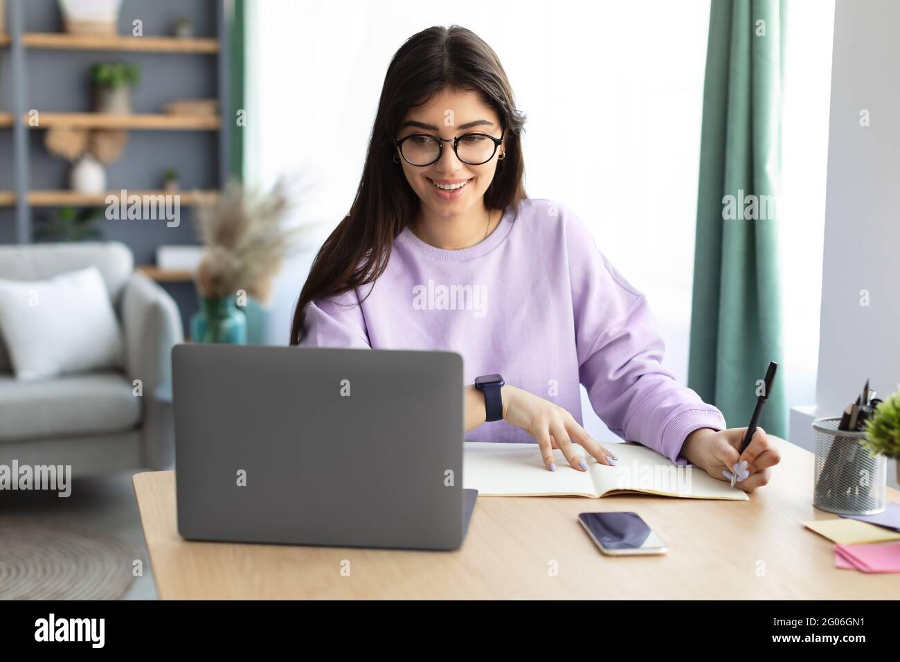 Woman sitting at desk, using computer writing in notebook Stock Photo ...