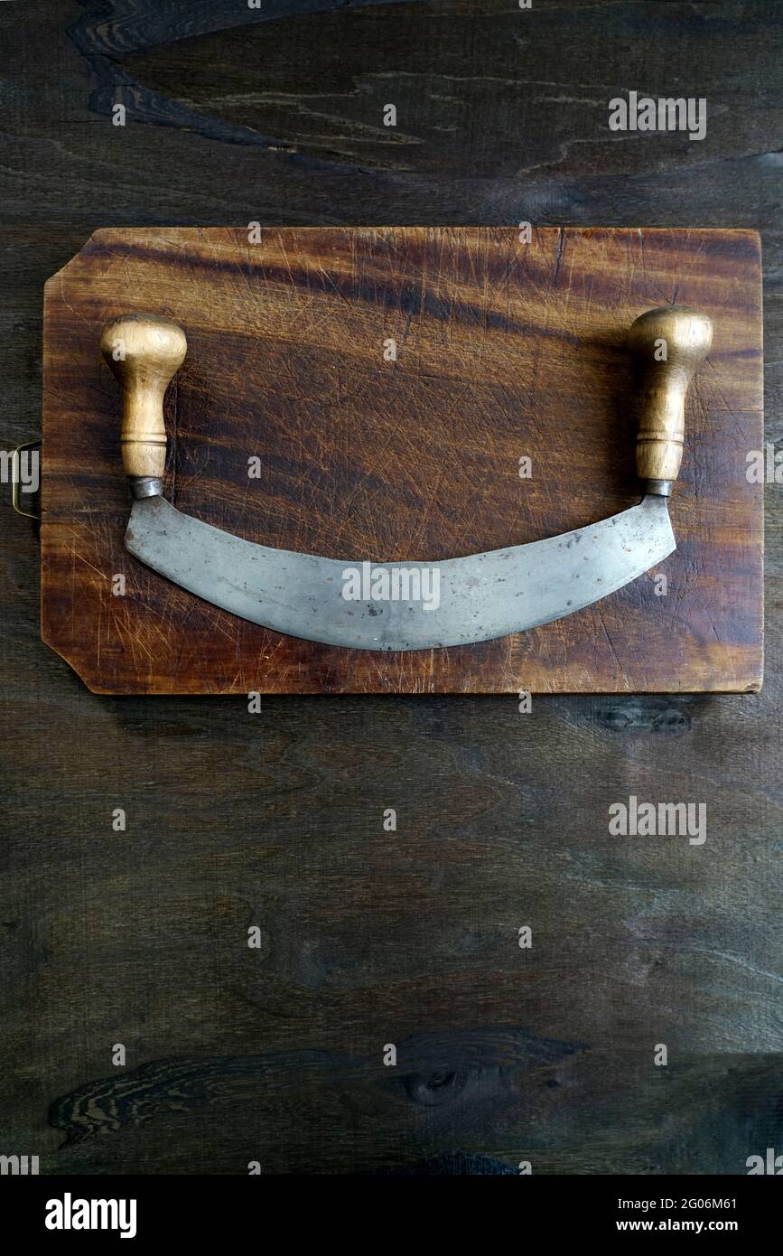 Old kitchen mezzaluna on a wooden cutting board on dark wooden ...