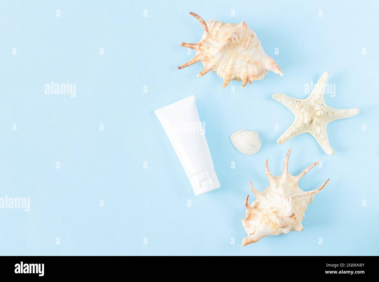 Blank unbranded white plastic cosmetic tube next to sea shells top view ...