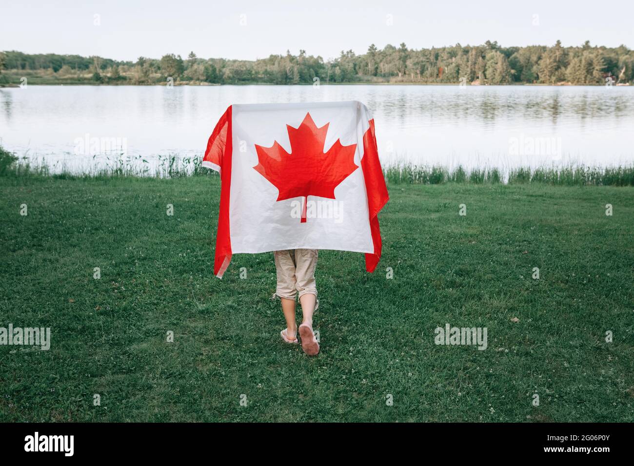 Girl wrapped in large Canadian flag by Muskoka lake in nature. Canada ...