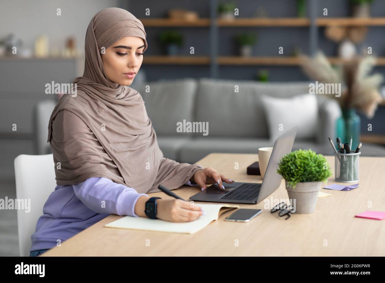 Muslim woman sitting at desk, using computer writing in notebook Stock ...
